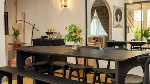 Uma área de jantar moderna com uma mesa comprida e várias cadeiras, um vaso decorativo com plantas e uma luminária fixada na parede.