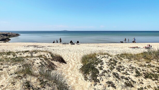 Uma praia com pessoas, céu claro e águas calmas.