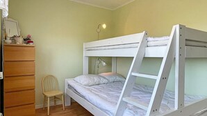Uma cama box com escada, uma cadeira de madeira e um armário em um quarto com paredes claras e piso de madeira.