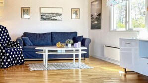 Sala de estar com sofá, mesa de centro e janela com cortinas. Quadros emoldurados na parede.