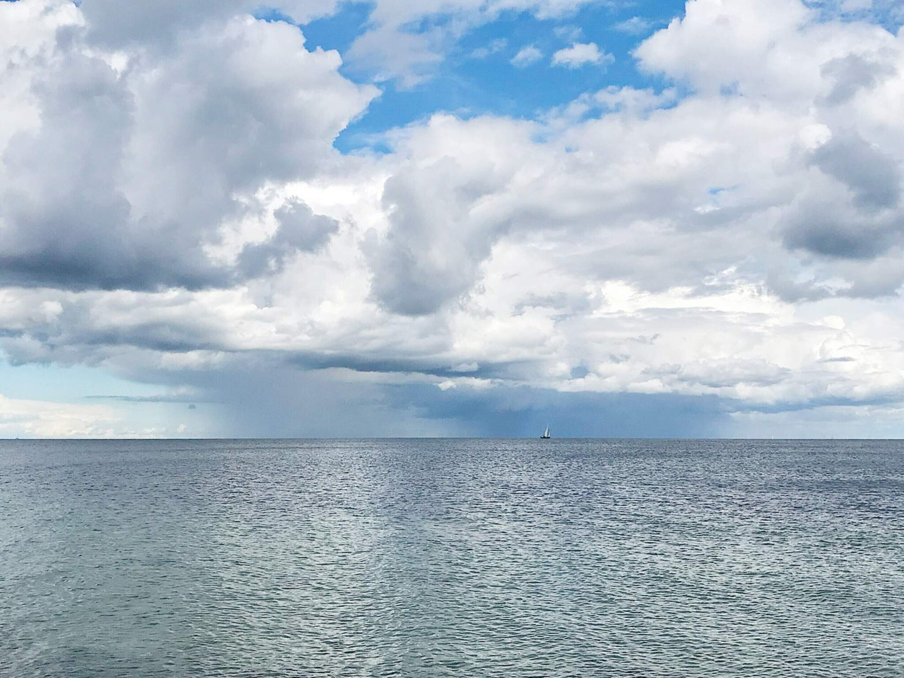 Vista de um mar calmo com um veleiro ao longe sob um céu nublado.