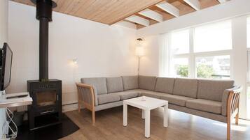 Uma sala de estar moderna com lareira embutida, sofá modular cinza, mesa de centro branca e uma grande janela que proporciona luz natural.