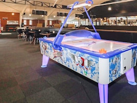 Uma mesa de hóquei no gelo em ambiente interno, com design azul e branco, cercada por cadeiras e mesas.