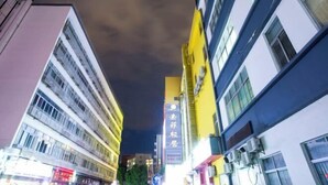Vista noturna de uma rua urbana com edifícios altos, incluindo um prédio amarelo de destaque com letreiros.