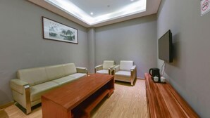 Uma sala de estar moderna com um sofá, duas poltronas, uma mesa de centro de madeira, uma televisão de tela plana na parede e um quadro emoldurado acima do sofá.