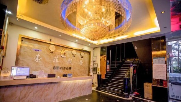 Uma área de recepção de hotel com balcão de mármore, um candelabro e uma escadaria que leva aos andares superiores.