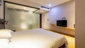 Quarto de hotel moderno com uma cama grande, uma divisória de vidro, uma televisão sobre uma estante de madeira e uma luminária fixada na parede.