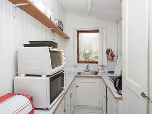 Cozinha compacta com armários brancos, micro-ondas, torradeira e janela com vista para o verde.