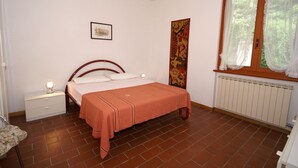 Quarto com cama, mesa de cabeceira, radiador e janela com cortinas.