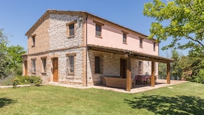 Uma casa de pedra de dois andares com varanda coberta e um pequeno jardim.