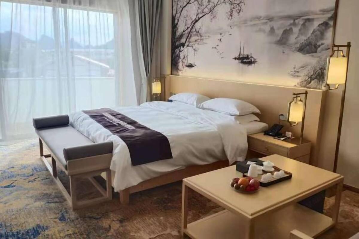 Quarto de hotel com cama, mesa de cabeceira, abajur e vista para o exterior.