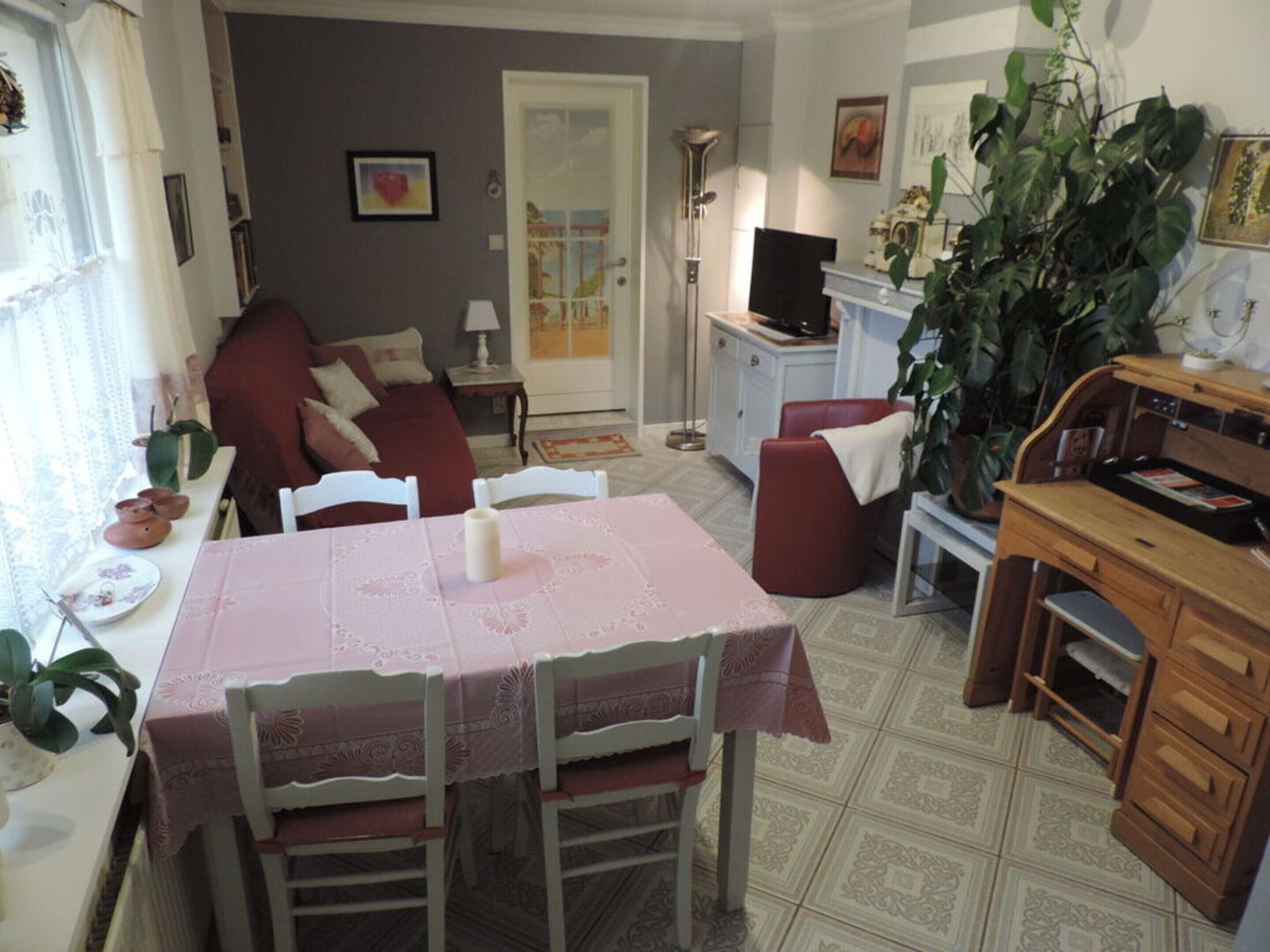 Uma sala de estar aconchegante com uma mesa de jantar, cadeiras, um sofá, uma televisão e uma planta grande.