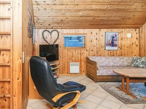 Interior acolhedor de uma cabana com teto de madeira, televisão, sofá e mesa de jantar.