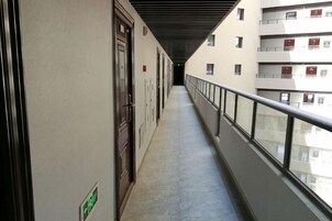 Um corredor com portas, corrimão e vista para um edifício com vários andares.
