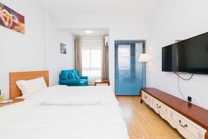 Quarto de hotel com cama, televisão, cadeira azul, cômoda de madeira e porta com persianas.
