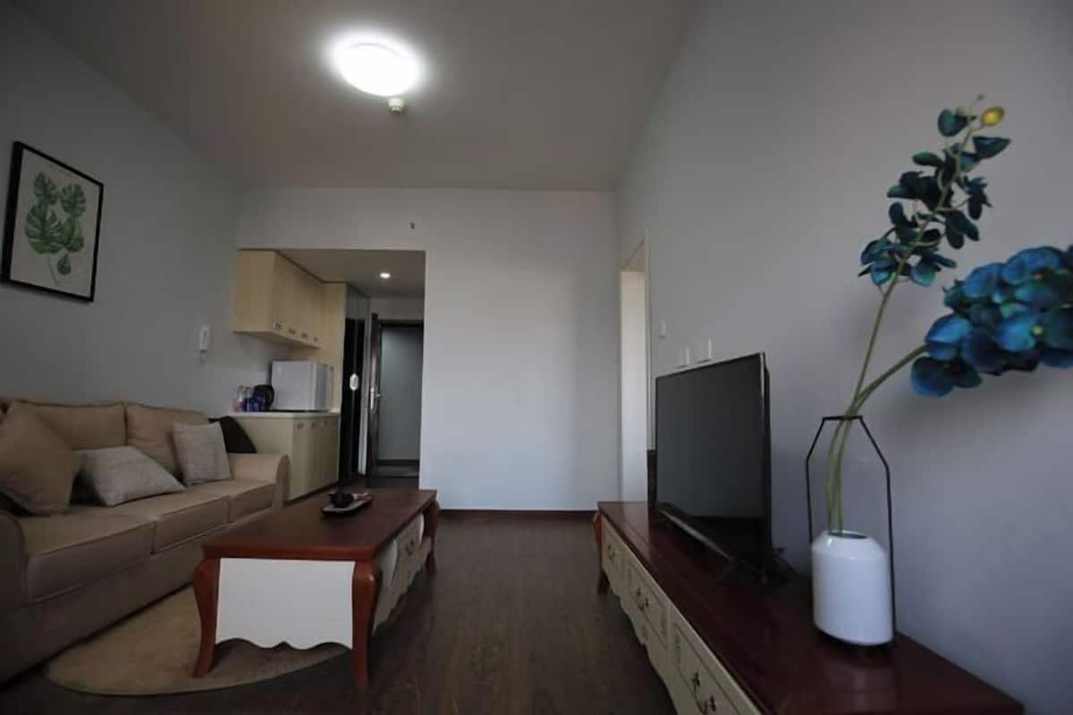 Sala de estar com sofá, mesa de centro, televisão de tela plana, armário de madeira e um vaso com flores.