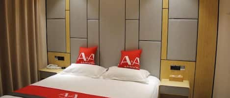 Quarto de hotel com uma cama grande, duas mesas de cabeceira, um telefone e uma pequena mesa de madeira com um cesto de lixo.