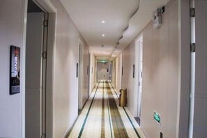 Corredor de hotel com portas em ambos os lados, um tapete estampado e uma lixeira no centro.