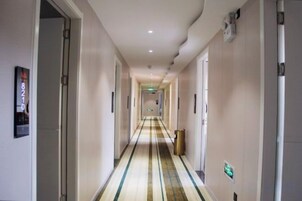 Corredor de hotel com portas em ambos os lados, um tapete estampado e uma lixeira no centro.