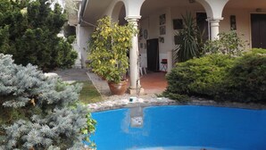 Um pátio com piscina, plantas em vasos e um edifício com arcos.