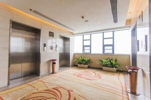 Área de elevadores com duas elevatórias, carpete estampado e plantas em vasos.