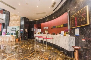 Uma área de recepção de hotel com piso de mármore, balcão de recepção e parede vermelha com quadros emoldurados.