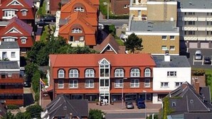 Uma vila costeira com uma mistura de edifícios residenciais, incluindo um hotel com telhado vermelho em destaque e um letreiro.