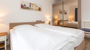 Quarto de hotel com uma cama grande, luminárias laterais, um espelho e um quadro na parede.