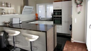 Cozinha moderna com ilha central, banquetas, forno duplo e lustre.