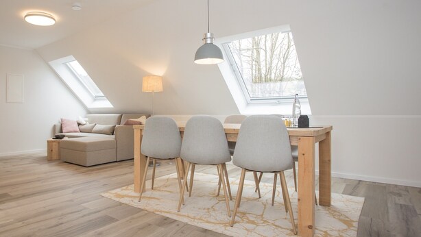 Quarto de loft moderno com claraboias, área de jantar com mesa e cadeiras de madeira, e um sofá.