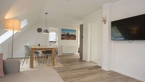 Uma sala de estar moderna com uma mesa de jantar de madeira, um sofá e uma TV fixada na parede.
