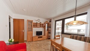 Uma sala de estar moderna com uma mesa de jantar de madeira, sofá vermelho e uma TV sobre um aparador de madeira.