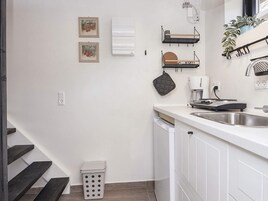 Cozinha moderna com armários brancos, pia de aço inoxidável, cafeteira e uma pequena lixeira.