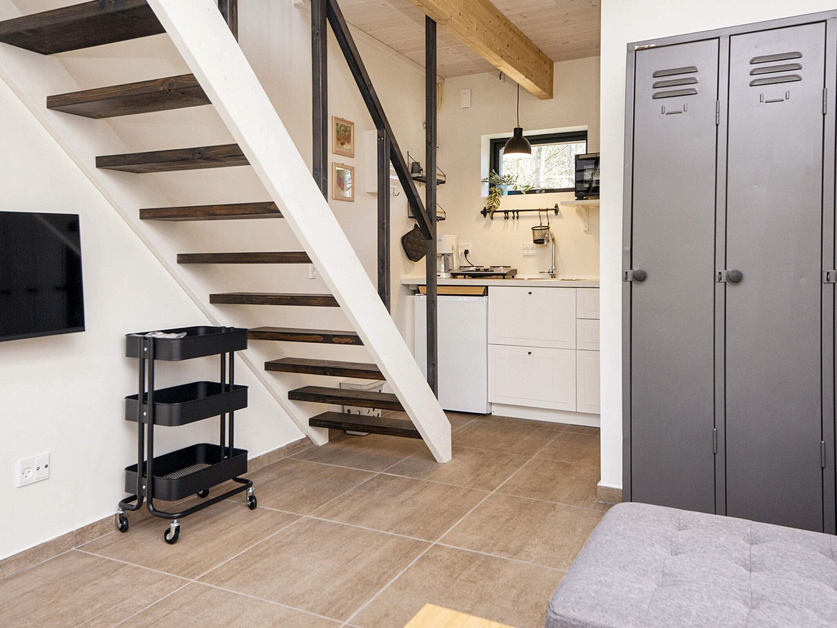 Uma escada leva a uma área de cozinha com uma mesa de jantar e um guarda-roupa cinzento.