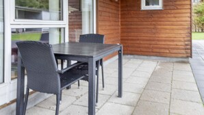 Um pátio externo com mesa e cadeiras, parede de madeira e uma janela.