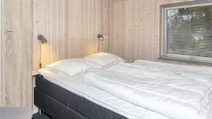Quarto com cama, duas luminárias de cabeceira, janela com persianas e paredes de madeira.