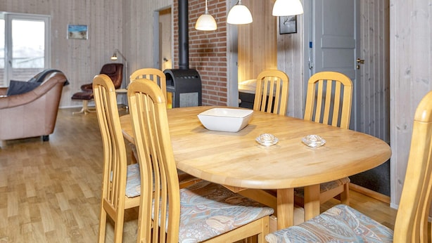 Uma sala de jantar com mesa redonda de madeira, seis cadeiras de madeira e duas luminárias pendentes.