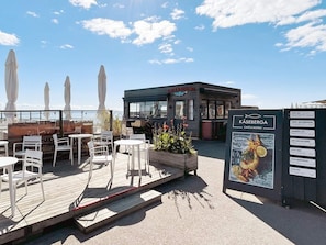 Café e bistrô com mesas ao ar livre, cardápio exposto e vista para o mar.