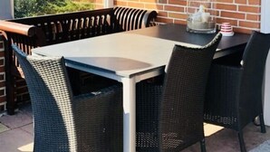 Uma varanda com mesa e cadeiras, um muro de tijolos e uma janela com vista para o verde.