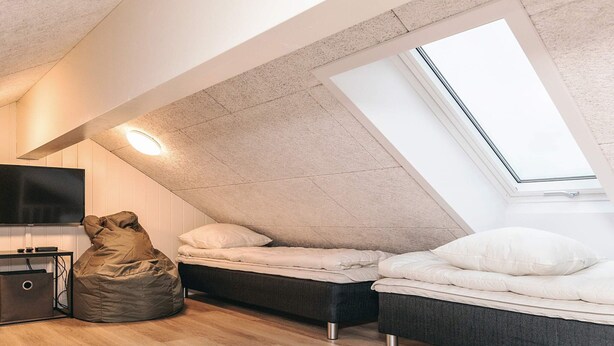 Quarto no estilo loft com teto inclinado, duas camas, uma poltrona de grãos, uma TV e um claraboia.