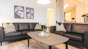 Uma sala de estar moderna com um sofá de couro escuro, uma mesa de centro redonda e arte abstrata na parede.