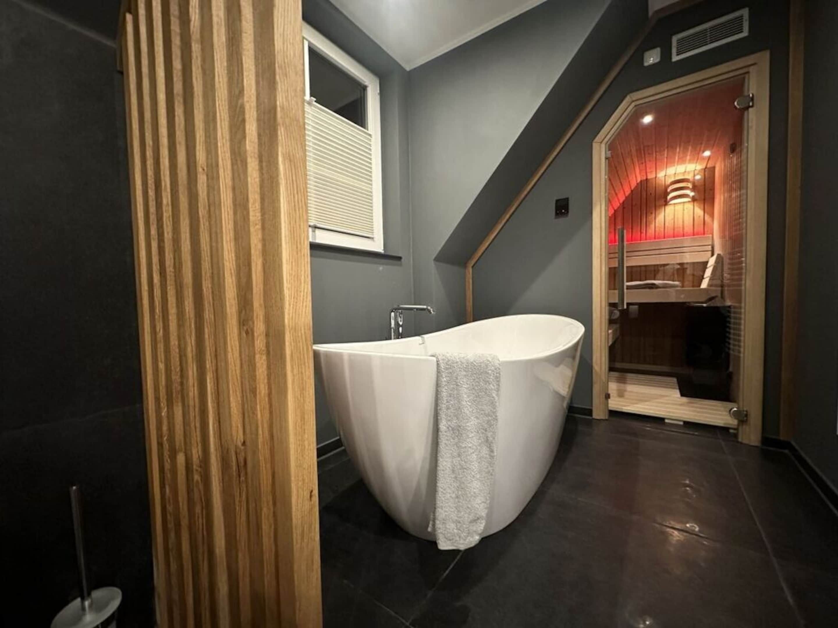 Um banheiro moderno com uma banheira de apoio, uma janela com persianas e uma área de sauna com iluminação vermelha.
