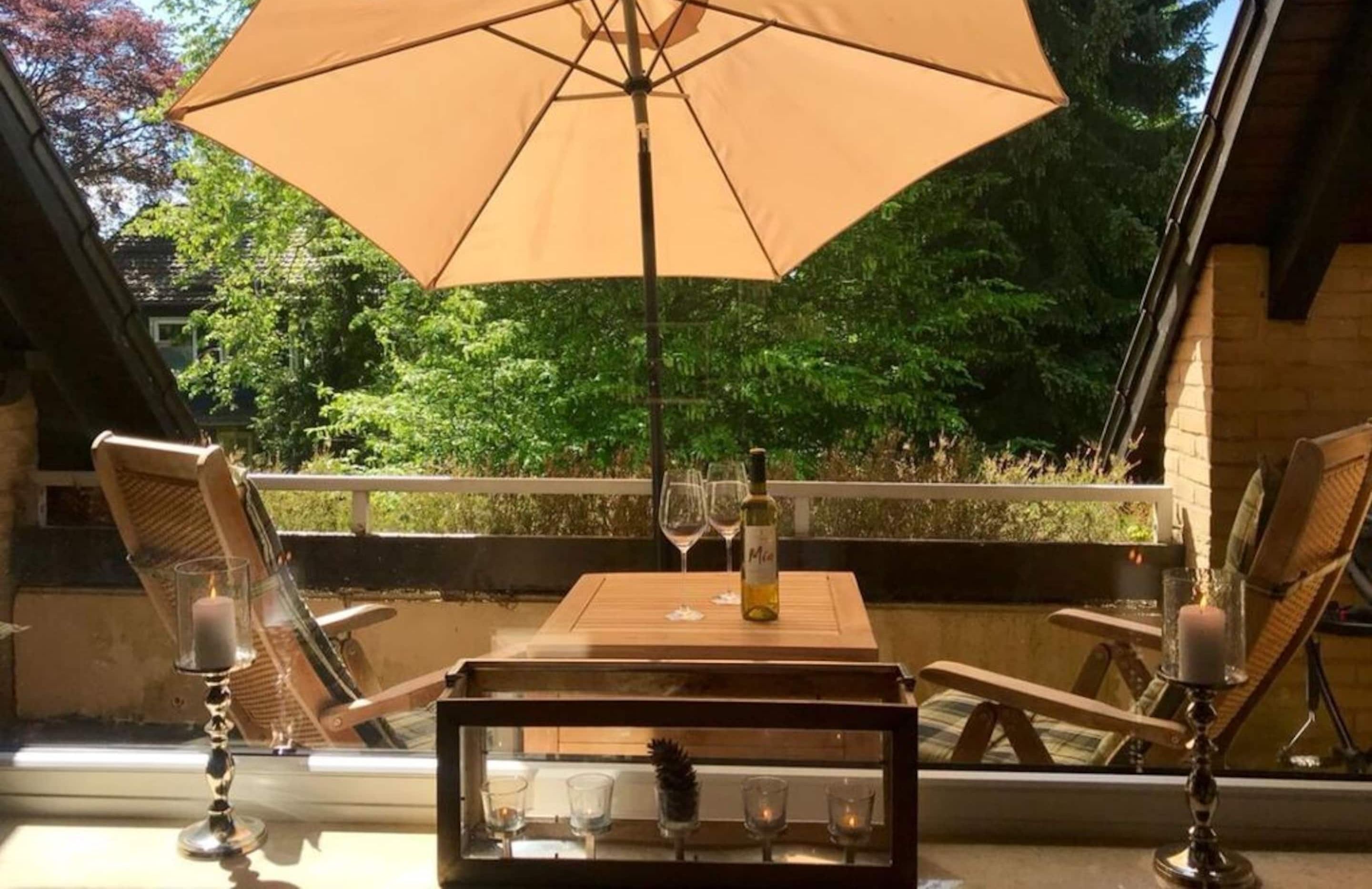 Uma área de refeições ao ar livre com mesa, cadeiras, um guarda-sol e velas.