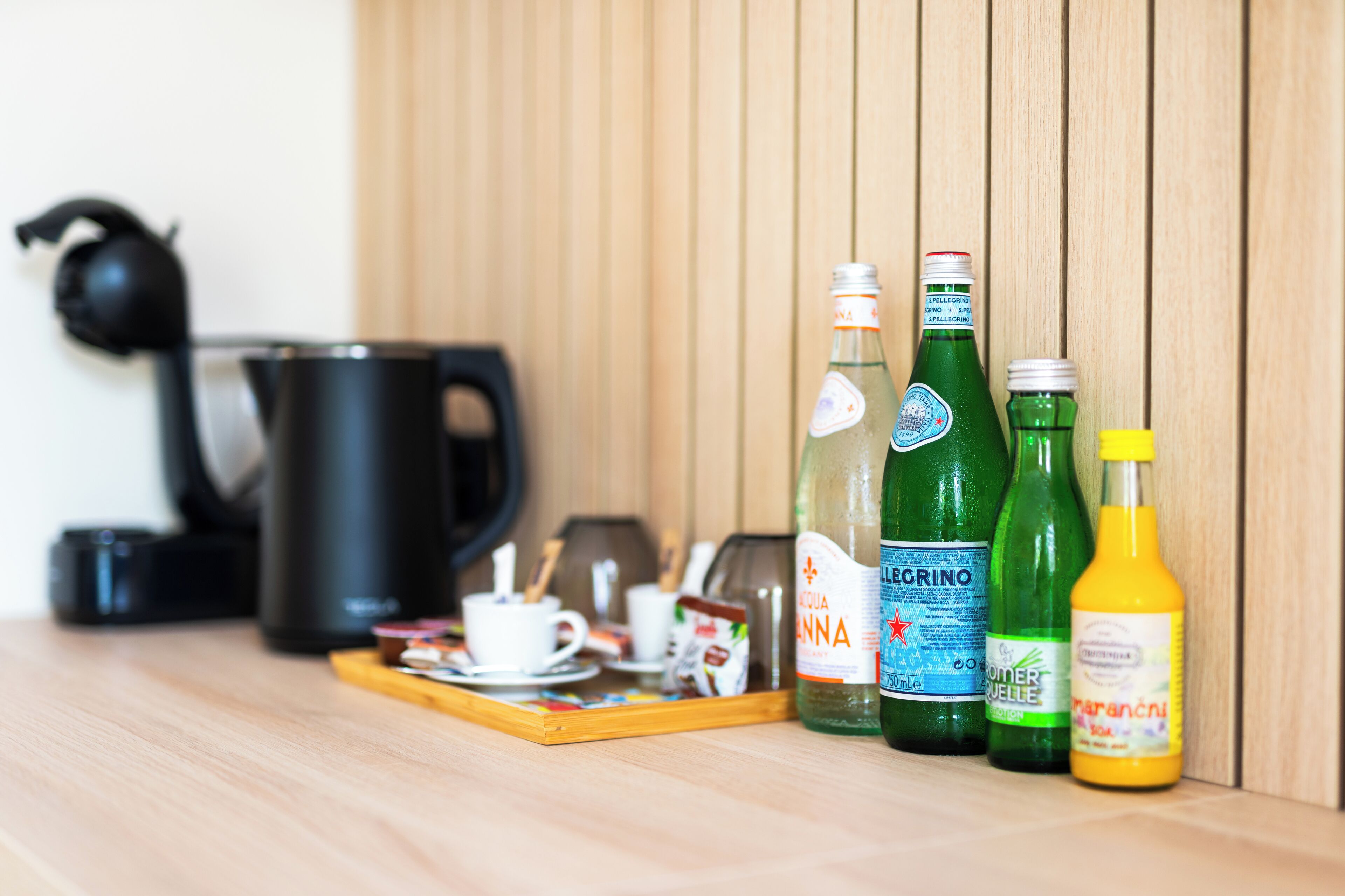Uma bancada de cozinha com cafeteira, chaleira e diversas garrafas de bebidas.