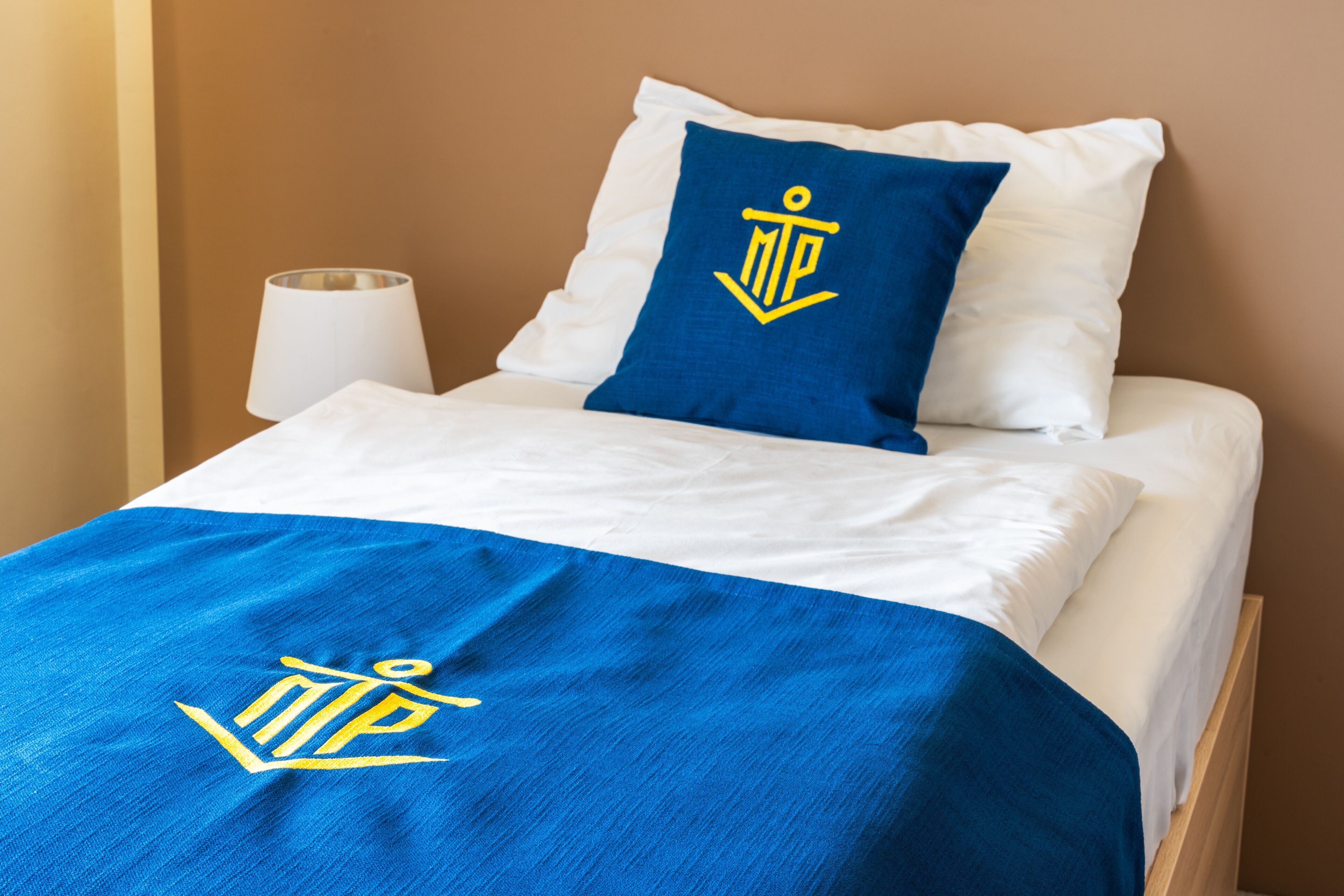 Cama com lençóis brancos e manta azul com um logotipo.