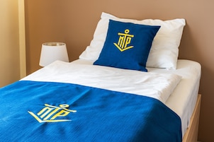 Cama com lençóis brancos e manta azul com um logotipo.