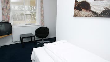 Quarto com cama, cadeira, mesa, televisão e janela com cortinas.