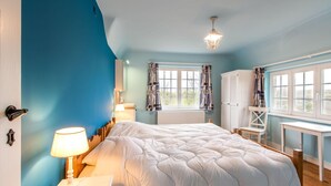 Quarto com cama, mesa de cabeceira, luminária, guarda-roupa e janela com cortinas.