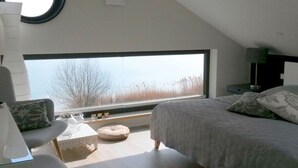 Quarto moderno com uma janela ampla, uma cama, uma cadeira e uma mesinha.