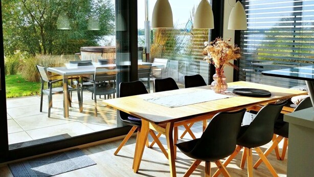 Uma sala de jantar moderna com uma mesa de vidro e cadeiras, um vaso com flores e vista para o exterior.